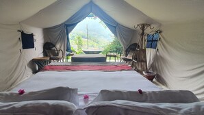 Acomodação em tenda com cama, cadeiras e vista para a paisagem.