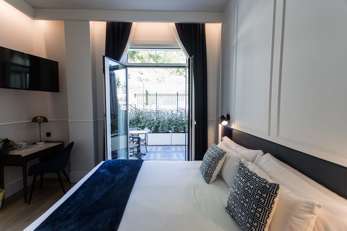 Quarto de hotel com cama, escrivaninha, cadeira, televisão e vista para o exterior.