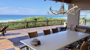 Uma área de refeições com vista para o oceano, um deck de madeira e um lustre.