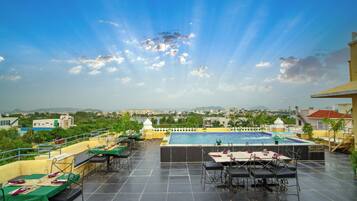 Uma área de piscina no terraço com mesas e cadeiras, vista para a cidade e céu limpo.