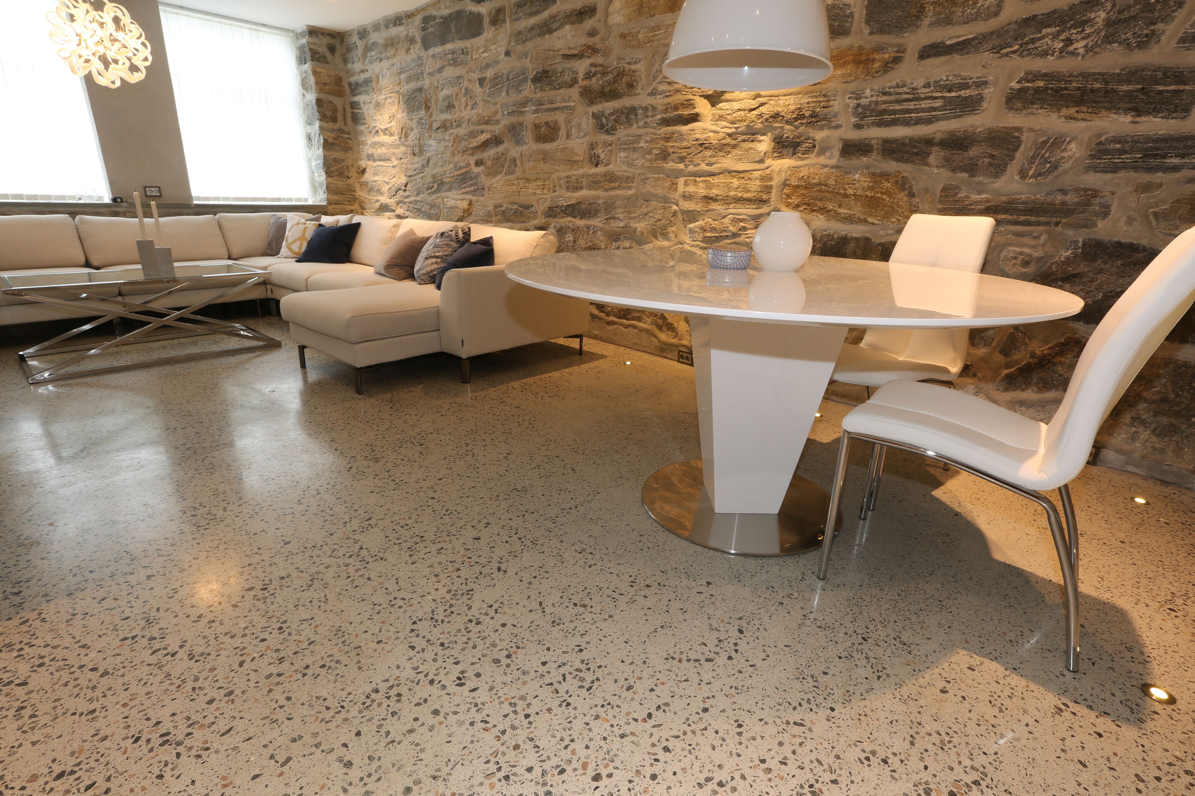 Uma sala de estar moderna com uma parede de pedra, uma mesa de jantar redonda com cadeiras brancas, um sofá com almofadas e uma mesa de centro de vidro.