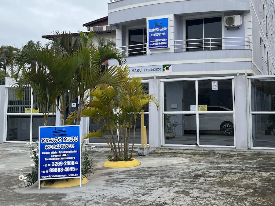 Um edifício com vários andares, varandas, uma placa e um carro estacionado.