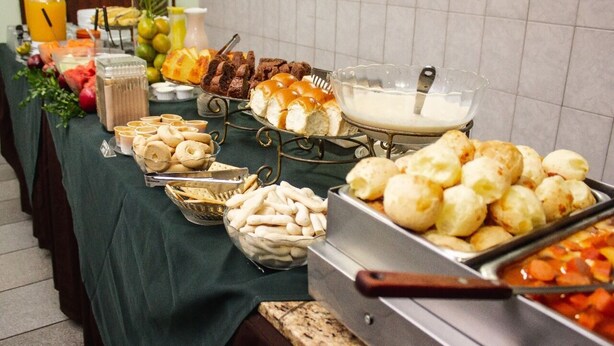 Uma mesa de buffet com diversos alimentos, incluindo doces, frutas e um dispensador de leite.