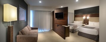 Quarto de hotel moderno com sofá, duas camas, televisão de tela plana e uma janela grande com cortinas.