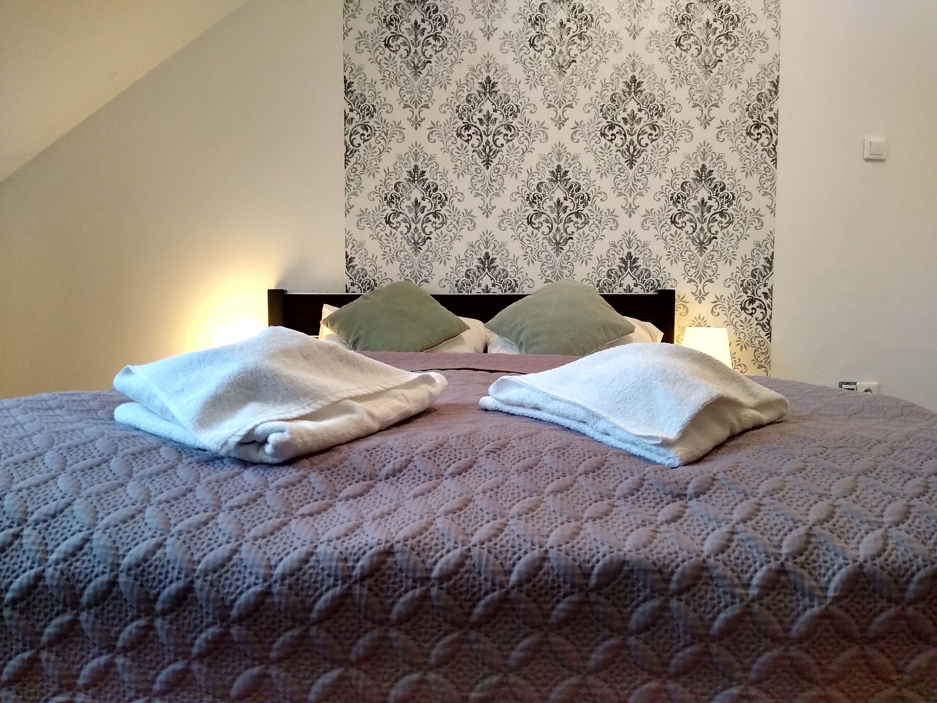 Cama bem arrumada com colcha estampada, duas almofadas e parede com papel de parede decorativo.