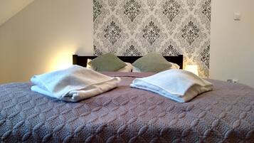 Cama bem arrumada com colcha estampada, duas almofadas e parede com papel de parede decorativo.