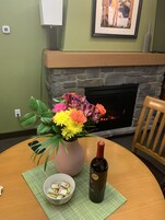 Uma mesa de jantar com um vaso de flores, uma garrafa de vinho e uma tigela de chocolates.