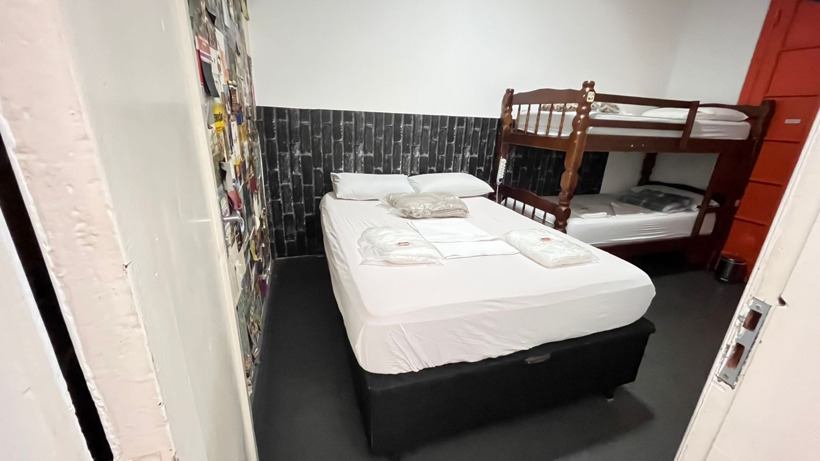Quarto pequeno e compacto com uma cama de solteiro, uma cama individual e uma parede decorada com diversos objetos.