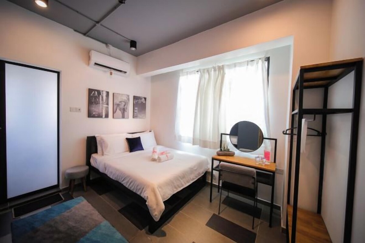 Quarto com cama, escrivaninha com cadeira, janela com cortinas e ar-condicionado fixado na parede.