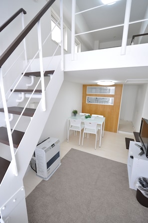 Um apartamento moderno com uma escada, uma área de jantar com mobiliário branco e uma cozinha.