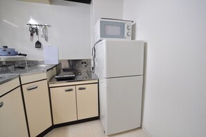 Uma cozinha compacta com geladeira branca, micro-ondas e bancada pequena.