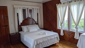 Uma cama bem arrumada com lençóis brancos, cabeceira de madeira e uma janela com cortinas.