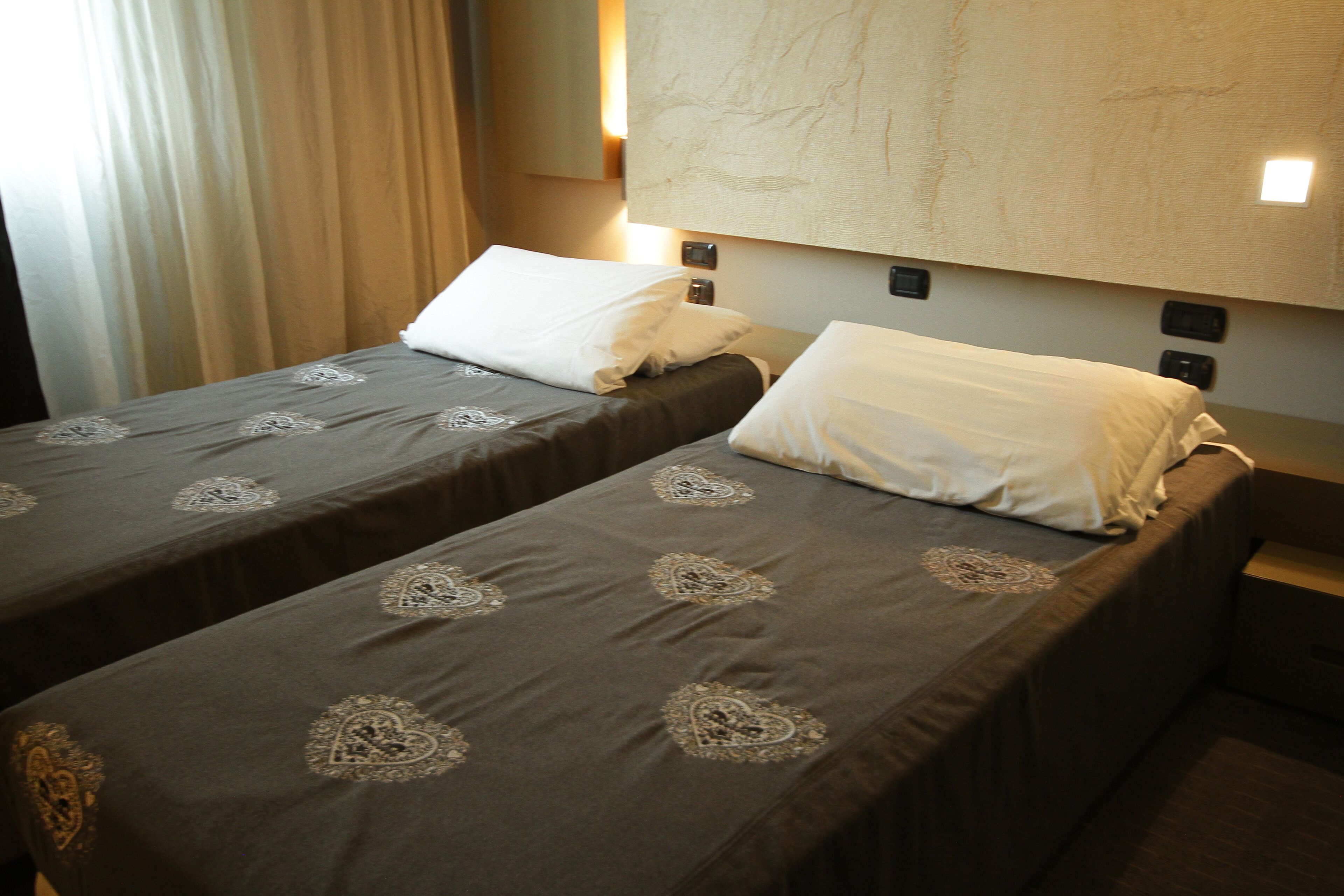 Duas camas de solteiro com cabeceiras combinando e almofadas decorativas, parede em tons neutros e janela com cortinas.