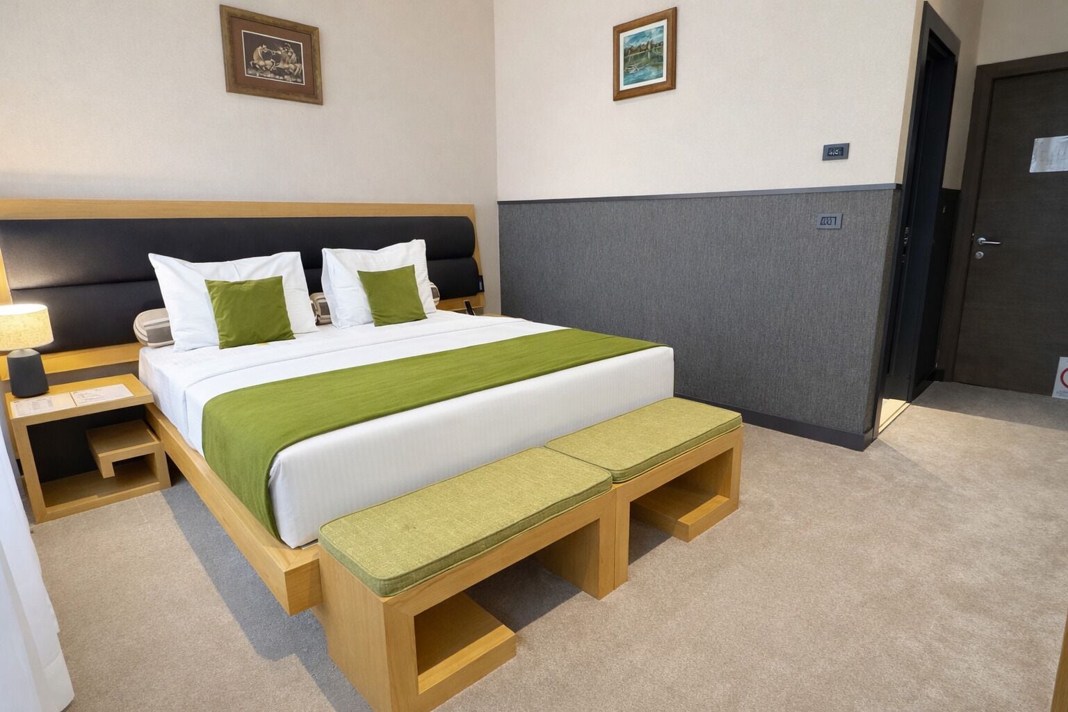 Quarto de hotel com cama, mesas de cabeceira, um banco e uma porta.