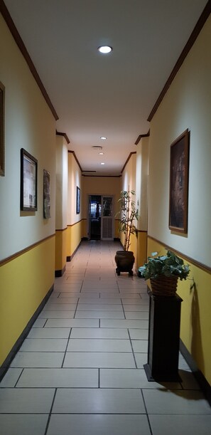 Um corredor com paredes amarelas, piso em azulejos e quadros nas paredes.