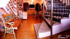 Uma escadaria com corrimão de ferro forjado, um banco de madeira e um sofá numa sala de estar com parede de tijolos e televisão de tela plana.