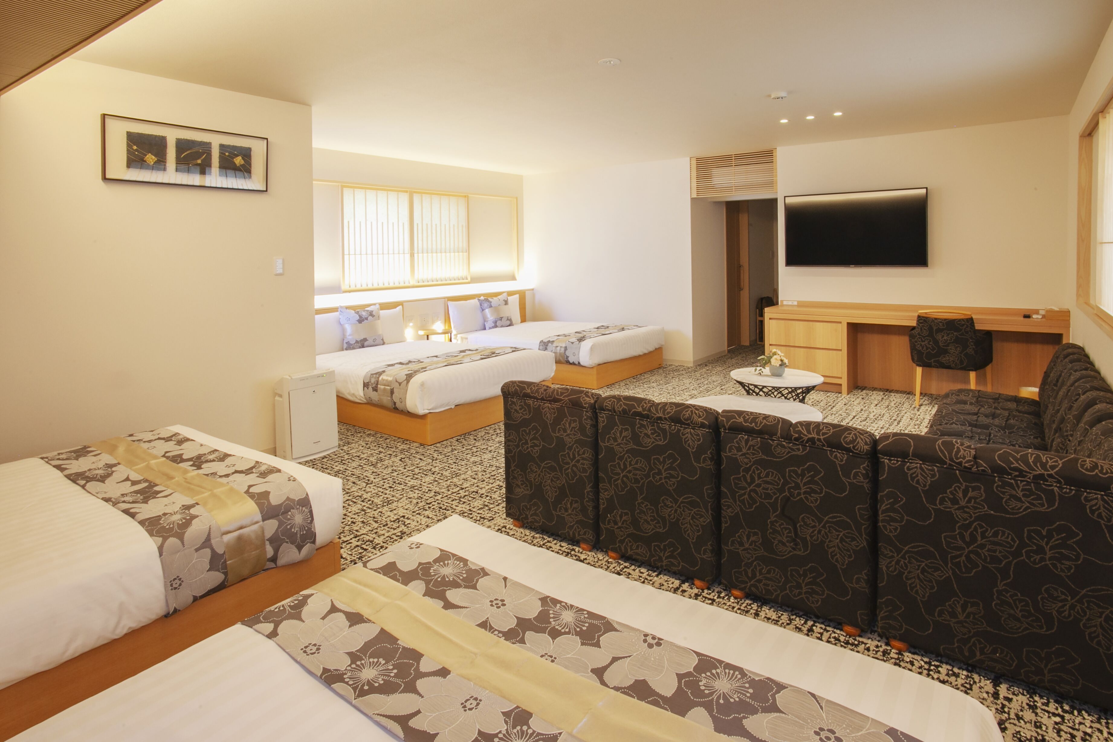 Quarto de hotel com duas camas, um sofá, uma televisão e uma escrivaninha.