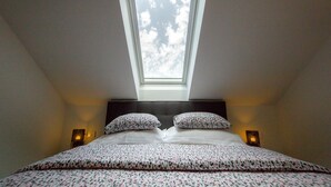 Quarto com claraboia, cama com duas almofadas e luminárias de cabeceira.