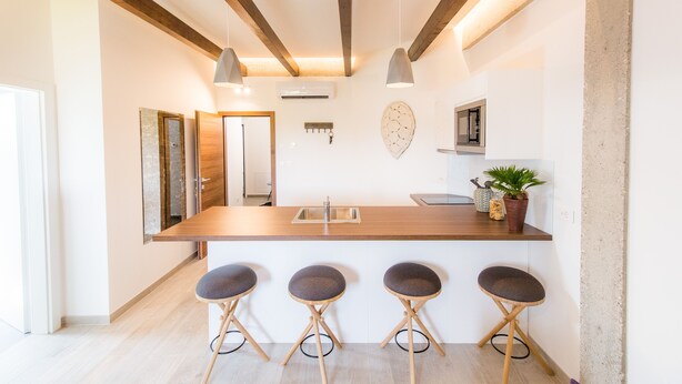 Cozinha moderna com ilha central, banquetas, iluminação pendente e vigas de madeira aparentes.