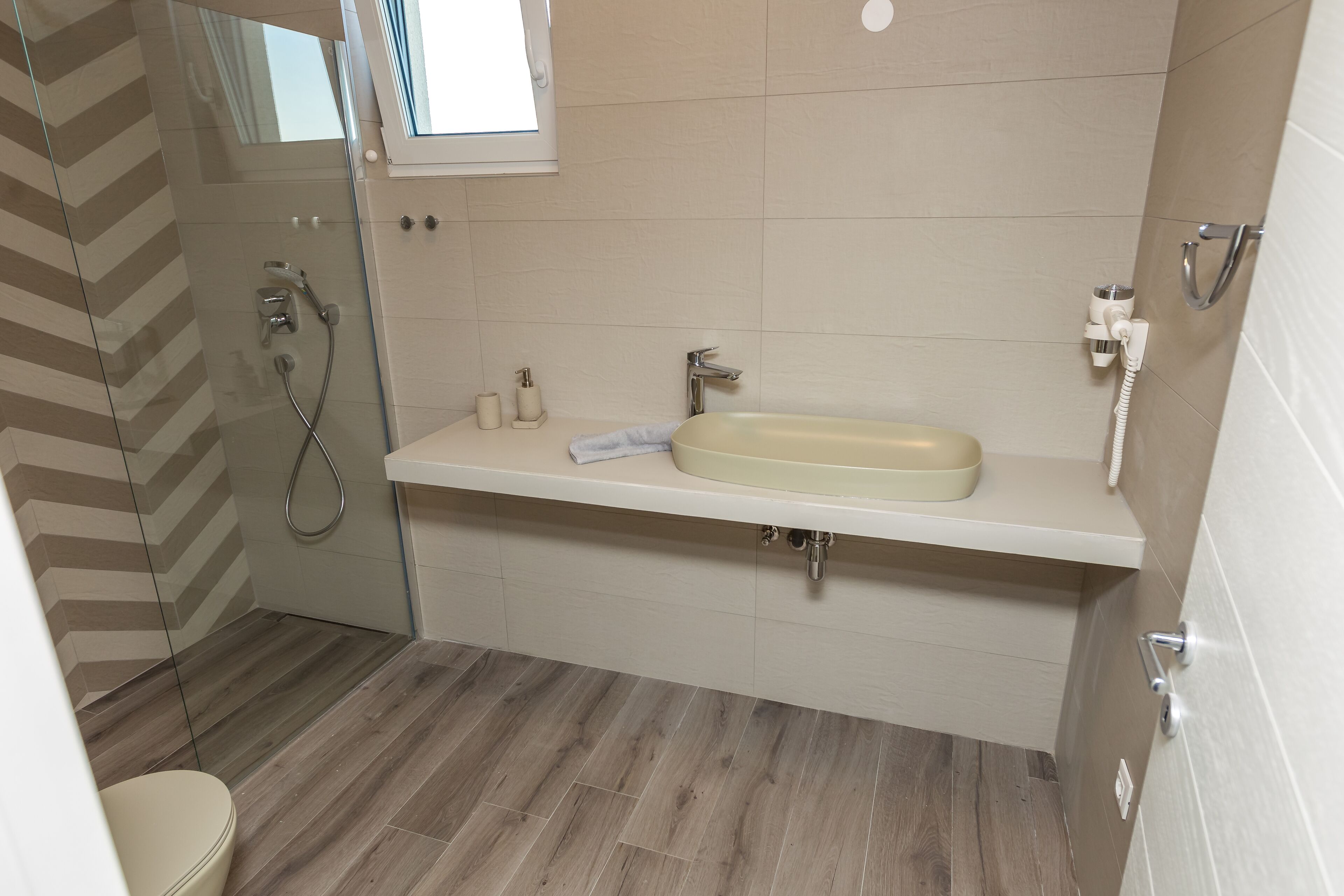 Uma casa de banho moderna com cabine de chuveiro em vidro, uma pia bege e uma sanita.