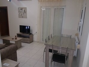 Sala de estar com televisão, sofá e mesa de centro. Há uma mesa de jantar com cadeiras e tampo de vidro.