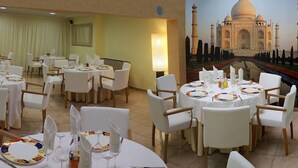 Restaurante com mesas redondas, cadeiras brancas e vista para o Taj Mahal.