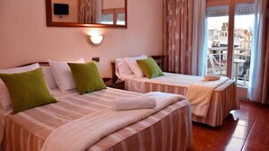Quarto de hotel com duas camas, um espelho grande, uma televisão e varanda com vista para a cidade.
