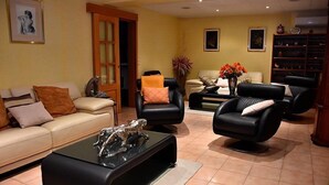 Uma sala de estar com um sofá bege, poltronas de couro preto, uma mesa de centro com uma escultura e uma estante de livros.