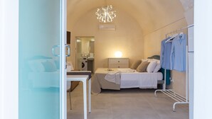 Quarto com cama, mesa de cabeceira, cabideiro e luminária no teto.