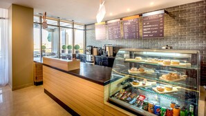 Interior moderno de uma cafeteria, com balcão, cardápios e uma vitrine com bolos e bebidas.