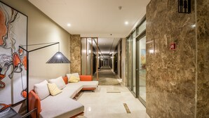Corredor de hotel com design moderno, com um sofá, uma lâmpada e uma parede de vidro.