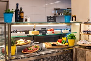Um balcão de buffet com diversos alimentos, incluindo queijo, tomates, azeitonas e uma seleção de carnes.
