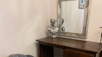 Quarto com cômoda de madeira, espelho e cadeira cinza.