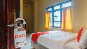 Quarto de hotel com cama, janela com cortinas, porta de madeira com placa e chão de azulejos.