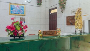 Uma receção com um letreiro que diz "RECEPTION", um relógio, um quadro emoldurado e um arranjo de flores.