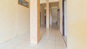 Um corredor com piso ladrilhado, paredes bege e um quadro pendurado à esquerda.