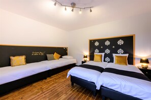 Quarto de hotel com duas camas de solteiro e uma cama de casal, chão de madeira e cabeceira com padrão preto e branco.