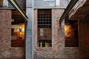 Vista interna de um edifício com paredes de tijolo, grades de metal e várias janelas com grades metálicas.