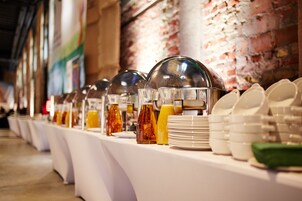 Disposição de buffet com diversos recipientes de comida e bebida, pratos e tigelas organizados sobre uma mesa.