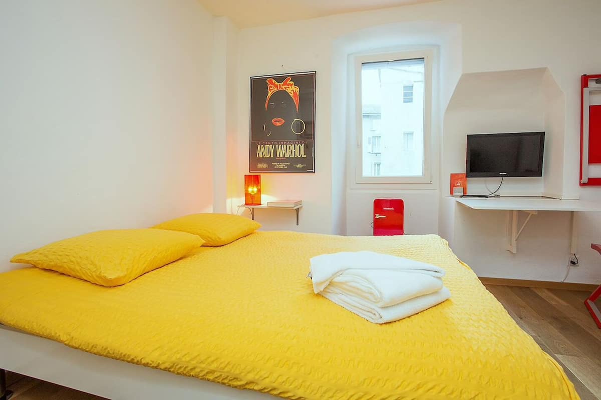 Quarto com cama, televisão, dispositivo Intermec vermelho e um cartaz na parede.