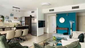 Uma sala de estar moderna com uma parede de destaque verde-água, uma mesa de centro de vidro e uma área de jantar com mesa e cadeiras de madeira.