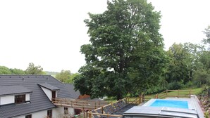 Uma casa com piscina, deck de madeira e uma grande árvore no quintal.
