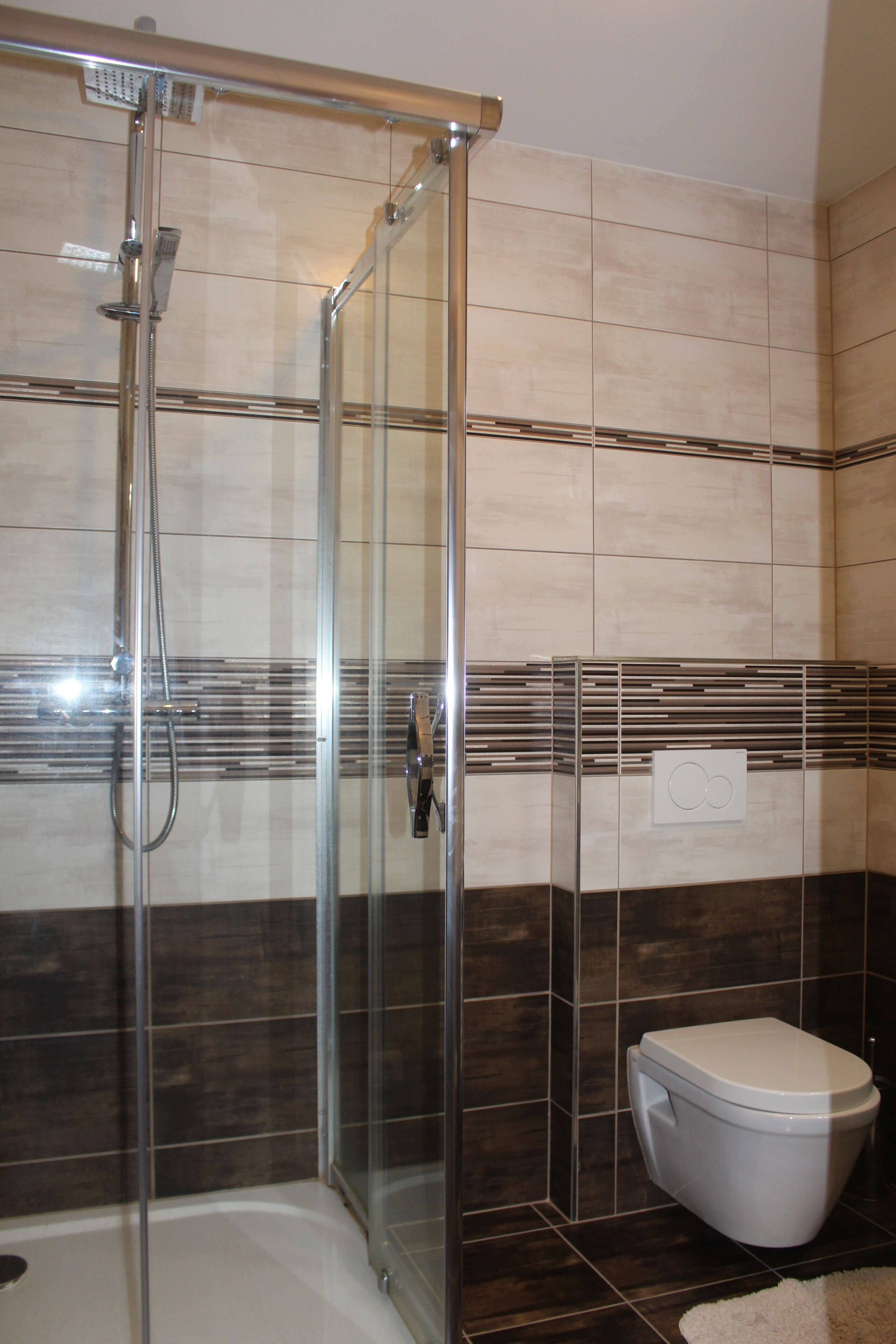 Uma casa de banho moderna com cabine de duche em vidro, sanita branca e painel de azulejos estampados.