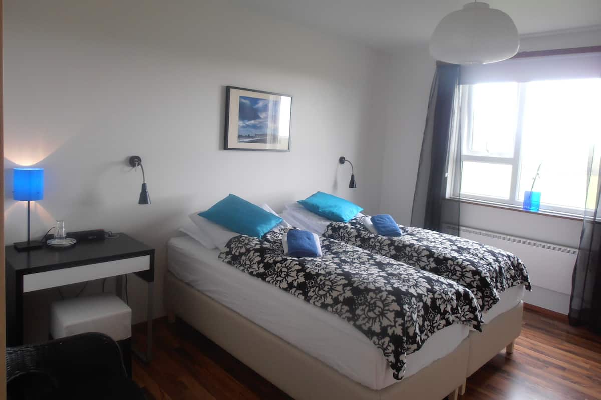 Quarto com duas camas, uma escrivaninha e uma janela com cortinas.