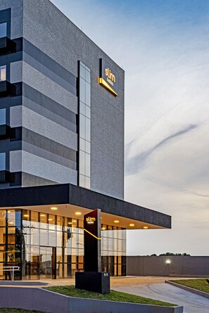 Um hotel moderno com um destaque para a placa 'Slim Hotels', grandes janelas de vidro e um design de telhado plano.
