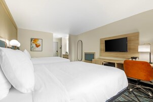 Quarto de hotel com uma cama grande, uma escrivaninha com computador, uma televisão e uma cadeira.