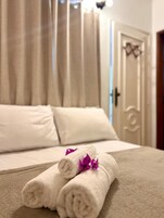 Cama bem arrumada com lençóis brancos e um par de toalhas com flores roxas em cima.