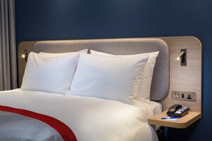 Quarto de hotel com uma cama, uma mesa de cabeceira com telefone e uma tomada.