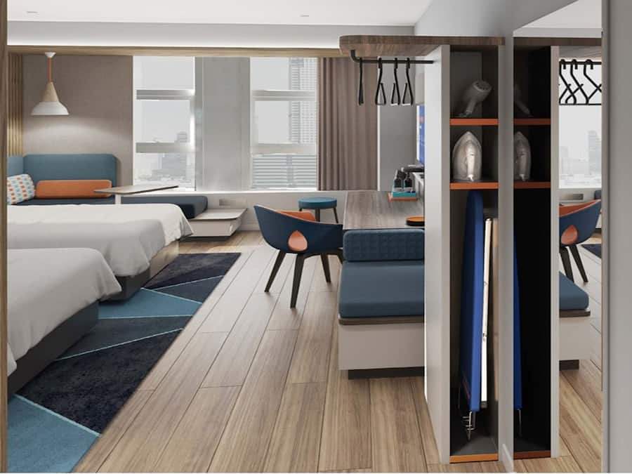 Quarto de hotel moderno com duas camas, área de refeições e guarda-roupa com espaço para pendurar roupas.