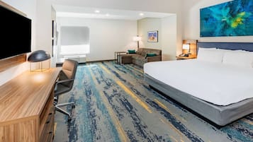Quarto de hotel com uma cama grande, uma escrivaninha com cadeira, um sofá, uma televisão e um quadro na parede.